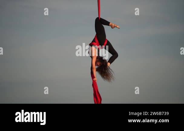 Female acrobat showing her flexibility and splits with red aerial silk ...