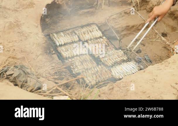 Woman feeding fire with coconut shells to grill fish on in-ground ...