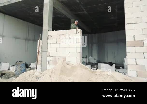 construction worker builds a white brick wall. The builder builds brick ...