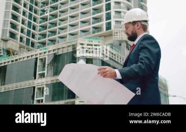 Engineer, male in a white safety helmet developer at a construction site checks on the drawings ...