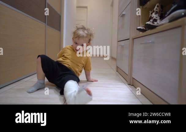 Smiling toddler with a cast on a broken leg crawls down the hallway of ...