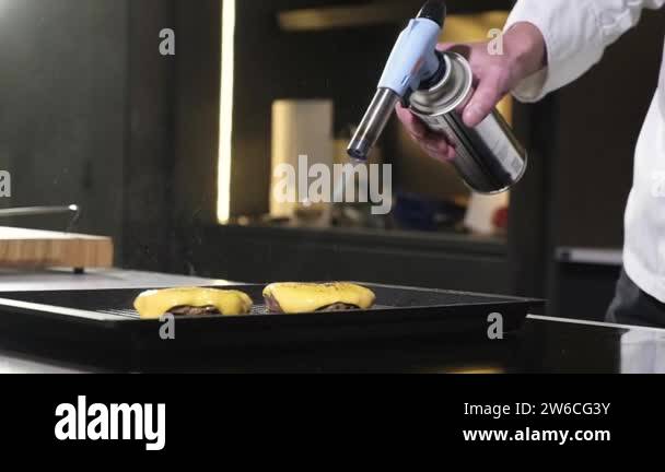 Cook in kitchen prepares meat beef patties with slices fresh cheese for ...