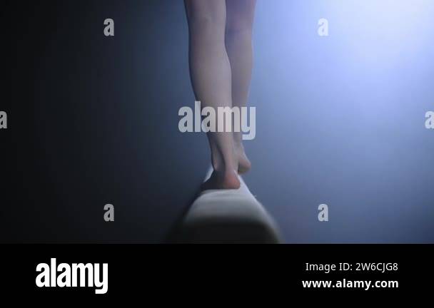 female gymnast on balance beam, closeup of legs, doing steps and jump ...