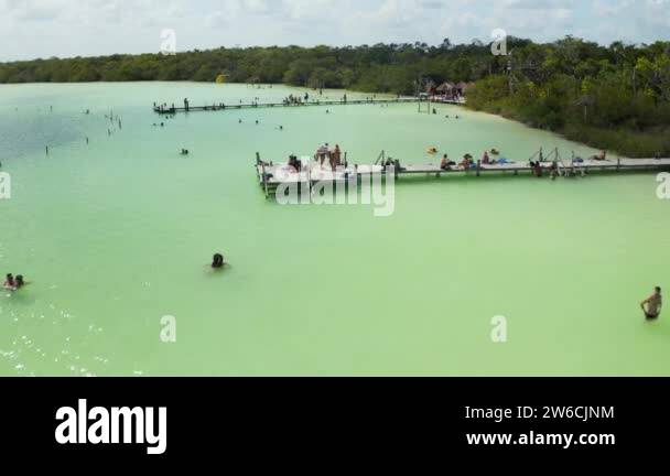 Fly over wooden piers at lake shore with people enjoying hot sunny day ...