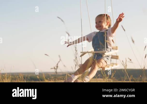 A small child is swinging high on a swing and laughing. The girl flies ...