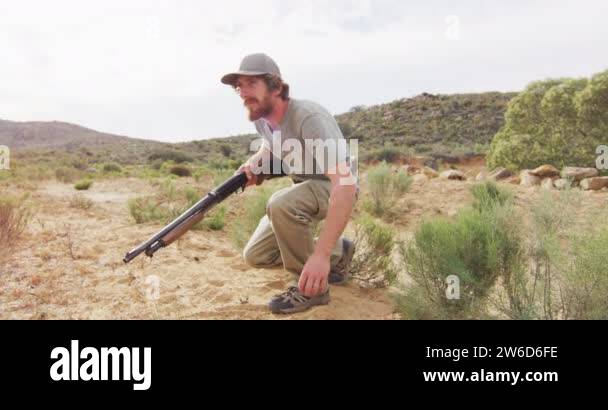 Kneeling caucasian male survivalist holding hunting rifle, examining ...