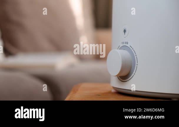 Woman turns on the modern air humidifier, aroma oil diffuser at home. Improving the comfort of ...