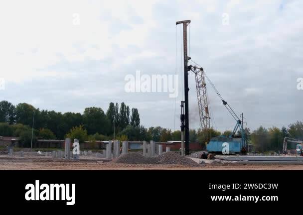 A large vertical pile-driving crane hammers reinforced concrete piles ...