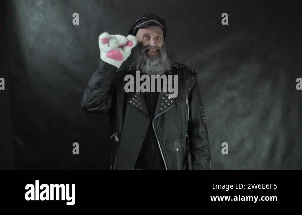 Bearded rocker in leather jacket and cap smiling and waving to audience ...