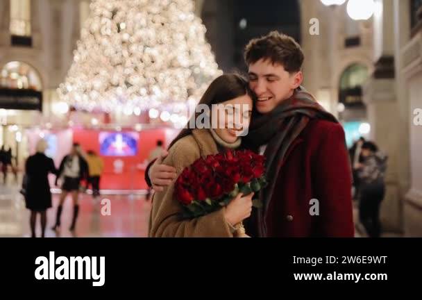 Young adult man with flowers kiss and hug his woman on the Christmas ...
