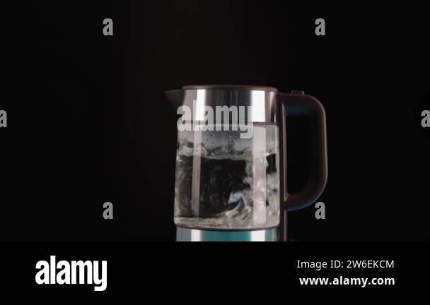 A modern glass electric kettle, black background, filled with water to ...