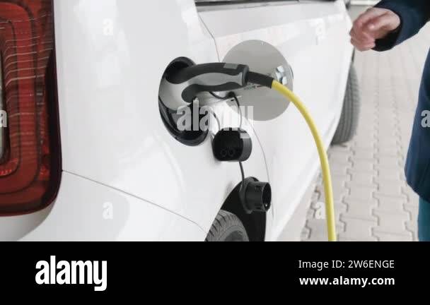 Woman opening the car and disconnecting the cable from an electric car ...