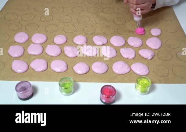Baker using a pastry bag to fill out circular shapes on parchment paper ...