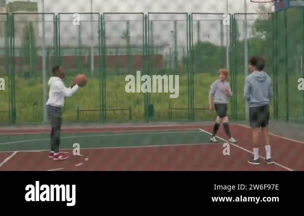 Handheld tracking shot from behind mesh netting fence of three guys ...