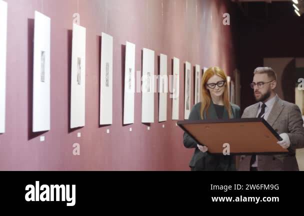 Female gallery manager pointing at wall and speaking with male ...