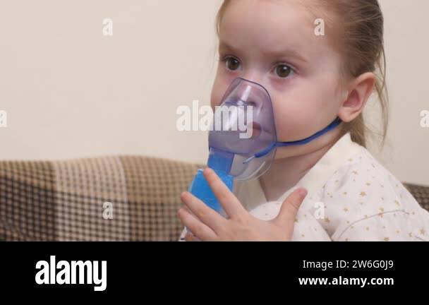 A cute baby in a mask is breathing through an inhaler. Home inhalation ...