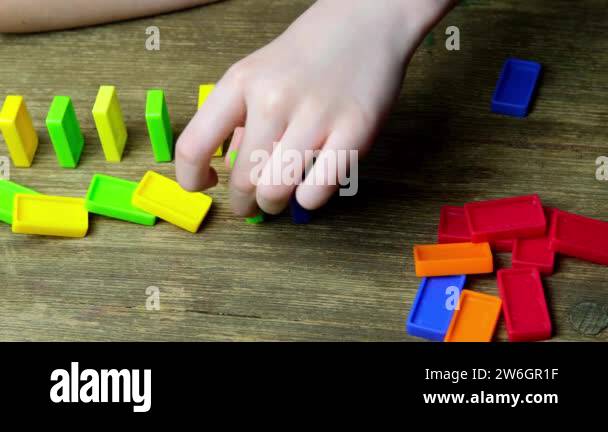 close-up of child's hand builds lines of dominoes, colored cubes of ...