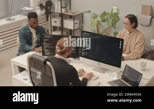 From-above slowmo shot of diverse male programmers team working on program coding sitting at one ...
