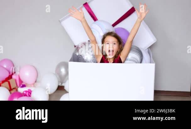 Cute, joyful little girl in pink dress jump out of the big present gift ...