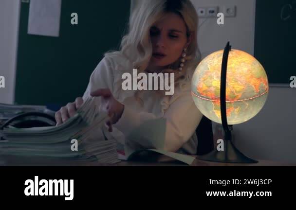 A tired school teacher checks notebooks in class late at night. The ...