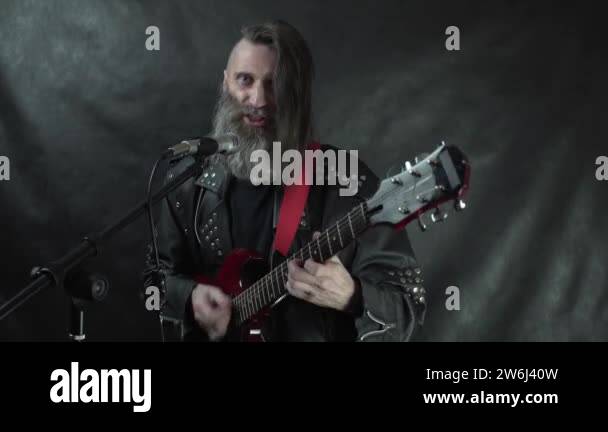 Bearded long-haired rock musician in leather jacket plays red electric ...