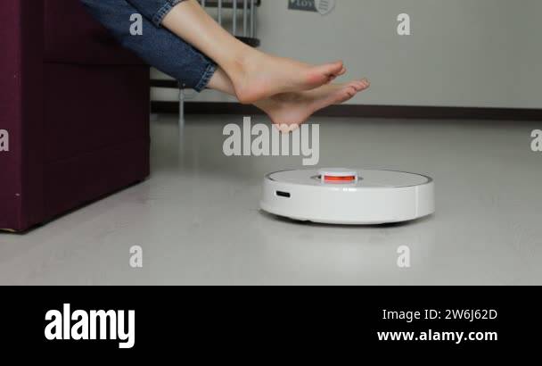 robot vacuum cleaner driving around barefoot woman at home. Female lift ...