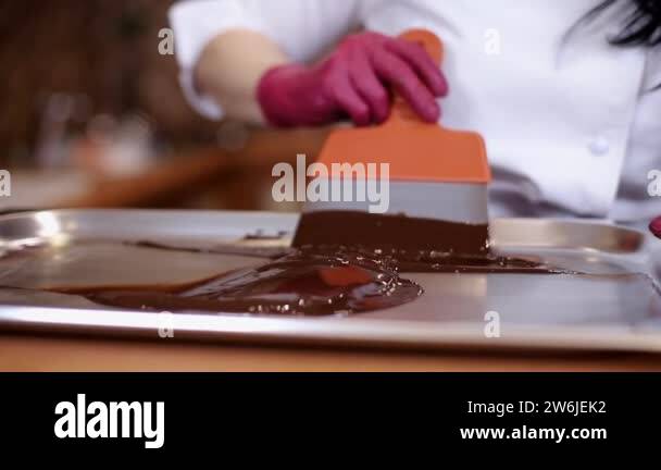 Confectioner is working with melted chocolate using putty knife. Woman ...