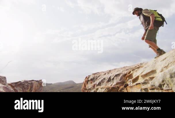 Bearded caucasian male survivalist with backpack jumping across rocky ...