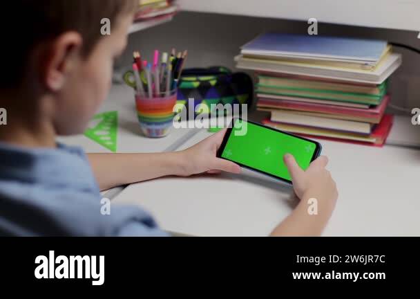 Boy holding a smartphone with a green screen at home, scrolling ...