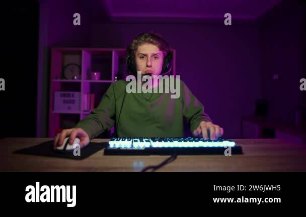 Sad gamer in a headset sits at a table at home at night and plays ...