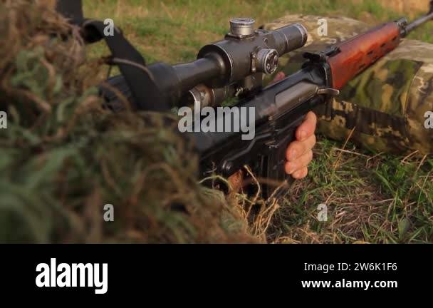 A sniper in a camouflaged sniper suit while lying down carries out ...