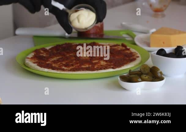 A man spreads mayonnaise on a base for a pizza smeared with tomato ...