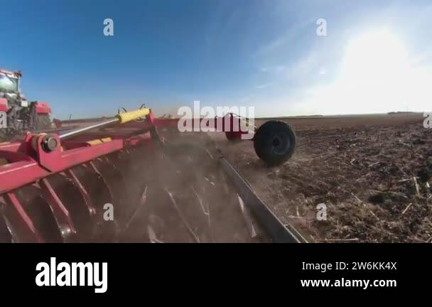 Back view of tractor with harrow system plowing ground on cultivated ...