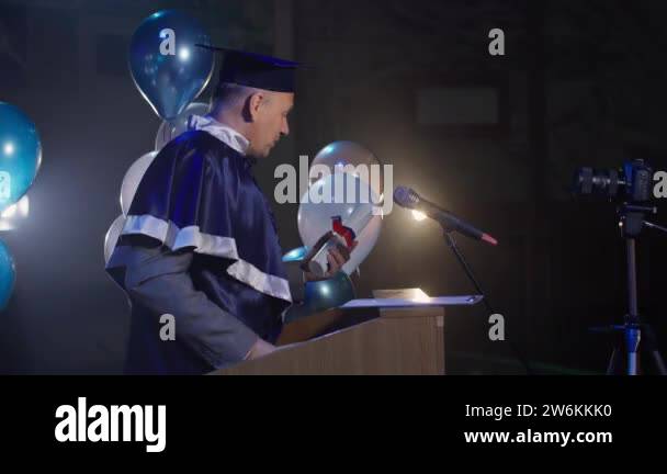 attractive male teacher wearing an academic cap and mantle conducts ...