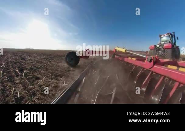 Back view of tractor with harrow system plowing ground on cultivated ...