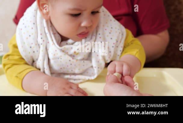 mother holds the baby in her arms and feeds her boy with a spoon ...