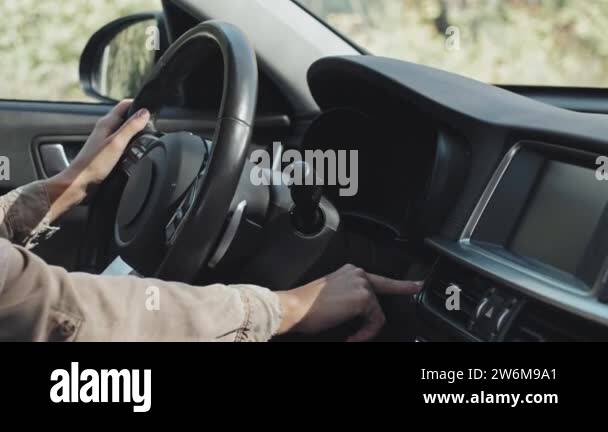 Tilt up shot of young Muslim woman in hijab sitting in car and pressing ...