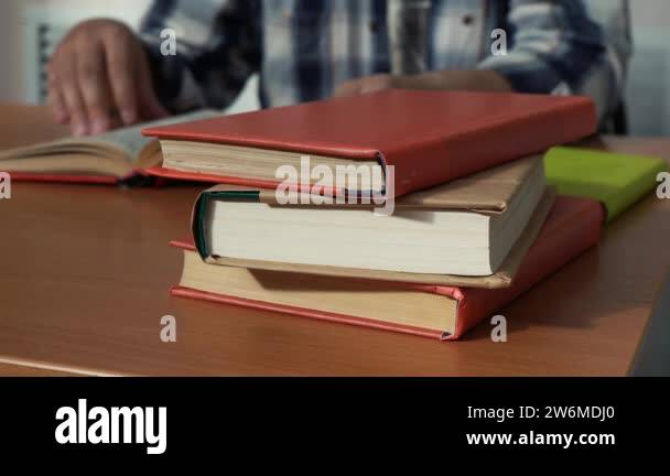a stack of books lying on the desk of a reading man in the library ...