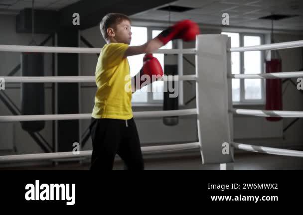 Little smiling boy in boxing gloves kicking the air on the boxing ring ...