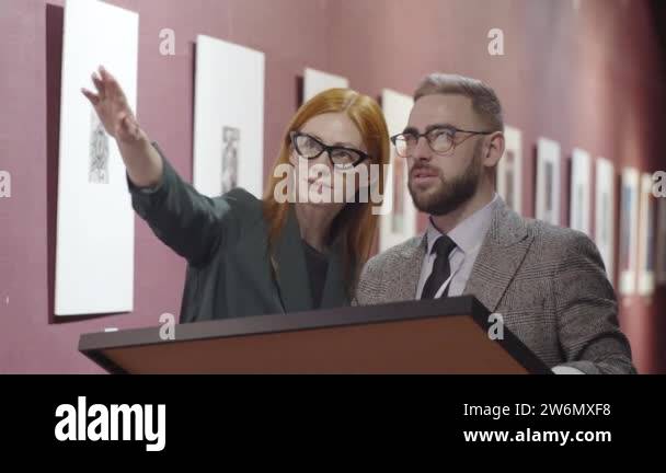 Female gallery manager pointing and telling to male colleague where to ...