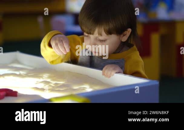 Cute child boy drawing draws developing sand in preschool at the table ...