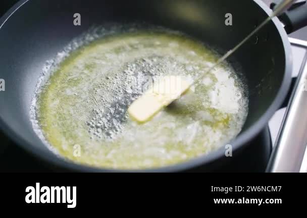Piece of golden butter slowly melts in heated black frying pan on ...