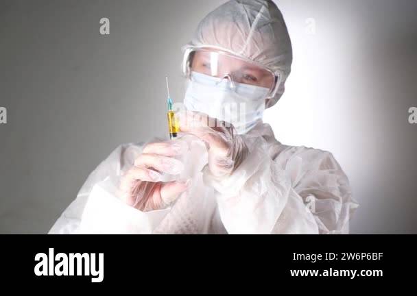 Female doctor wearing a medical mask and gloves prepares a pre-filled ...