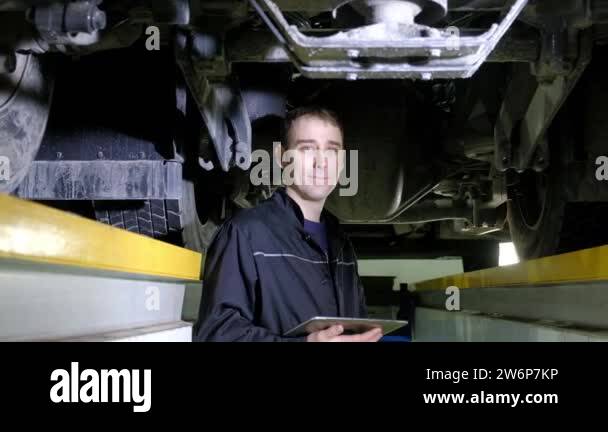 Positive young mechanical engineer stands under truck with tablet to ...