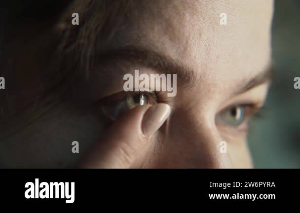 Slow motion macro of green or gray eye of a girl. A finger gently places a dirty contact lens ...