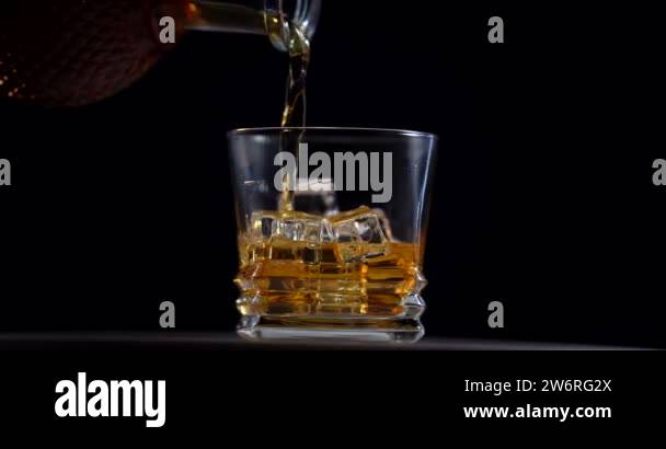 Golden whiskey pouring in the glass from the bottle. With ice cubes ...