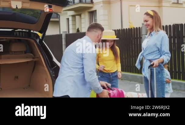 Family going on journey together. Dad packing luggage in trunk, giving ...