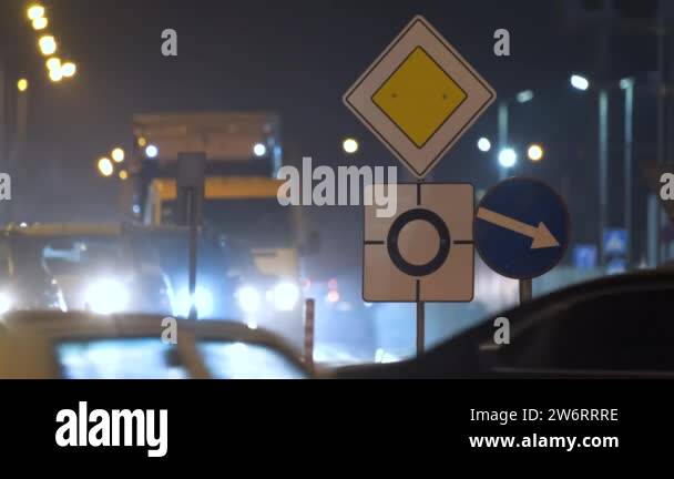 Roundabout road signs with blurred cars on city street traffic at night ...