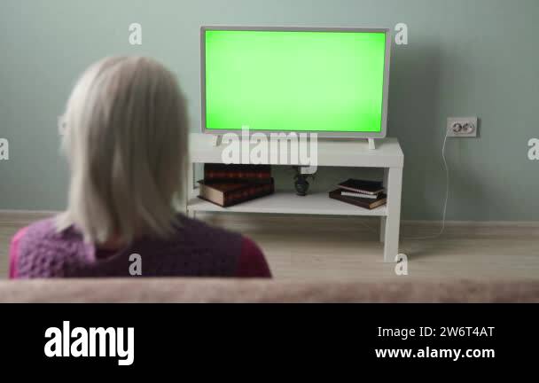 Grandma is watching TV. Green screen. A grandmother with gray hair sits ...