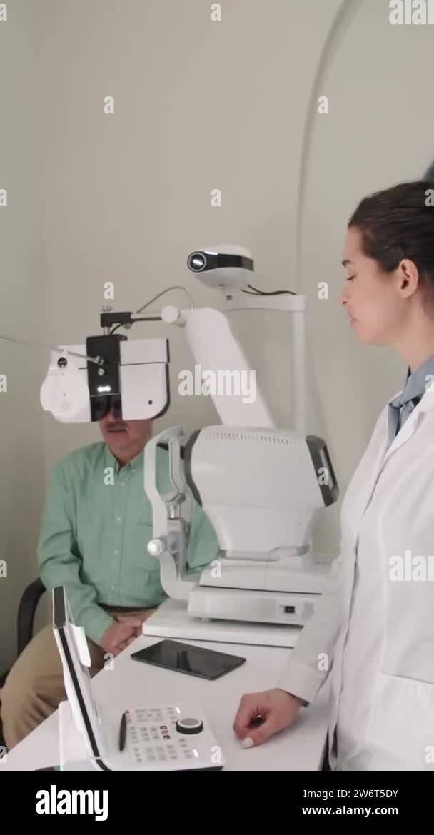 Vertical medium shot of young female optometrist using ophthalmic eye ...